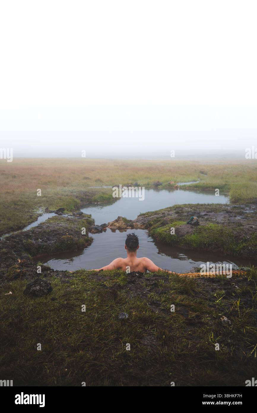 Young man lies in a natural Icelandic hot spring, surrounded by a misty ...