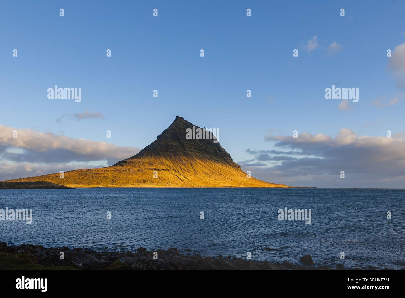 Kirkjufell mountain at sunrise with golden grasslands and soft clouds ...