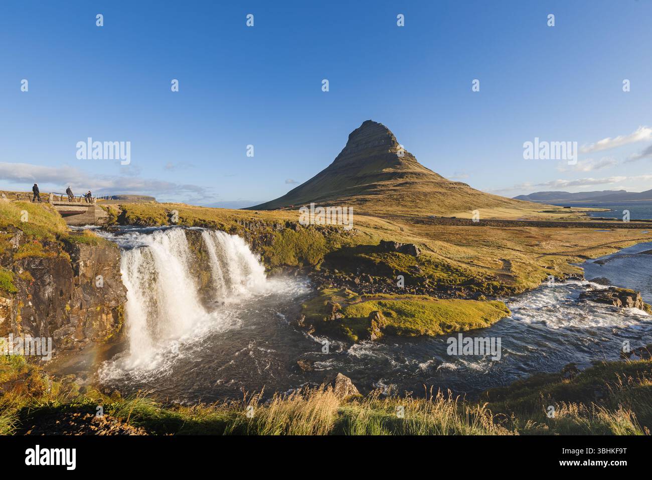 Kirkjufell mountain at sunrise with golden grasslands and soft clouds above, creating a peaceful ...
