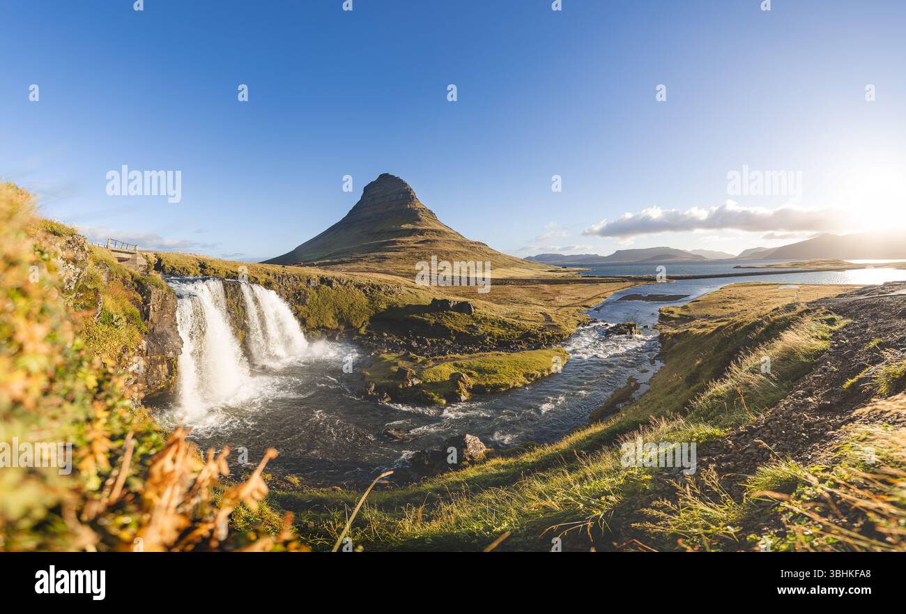 Kirkjufell mountain at sunrise with golden grasslands and soft clouds ...