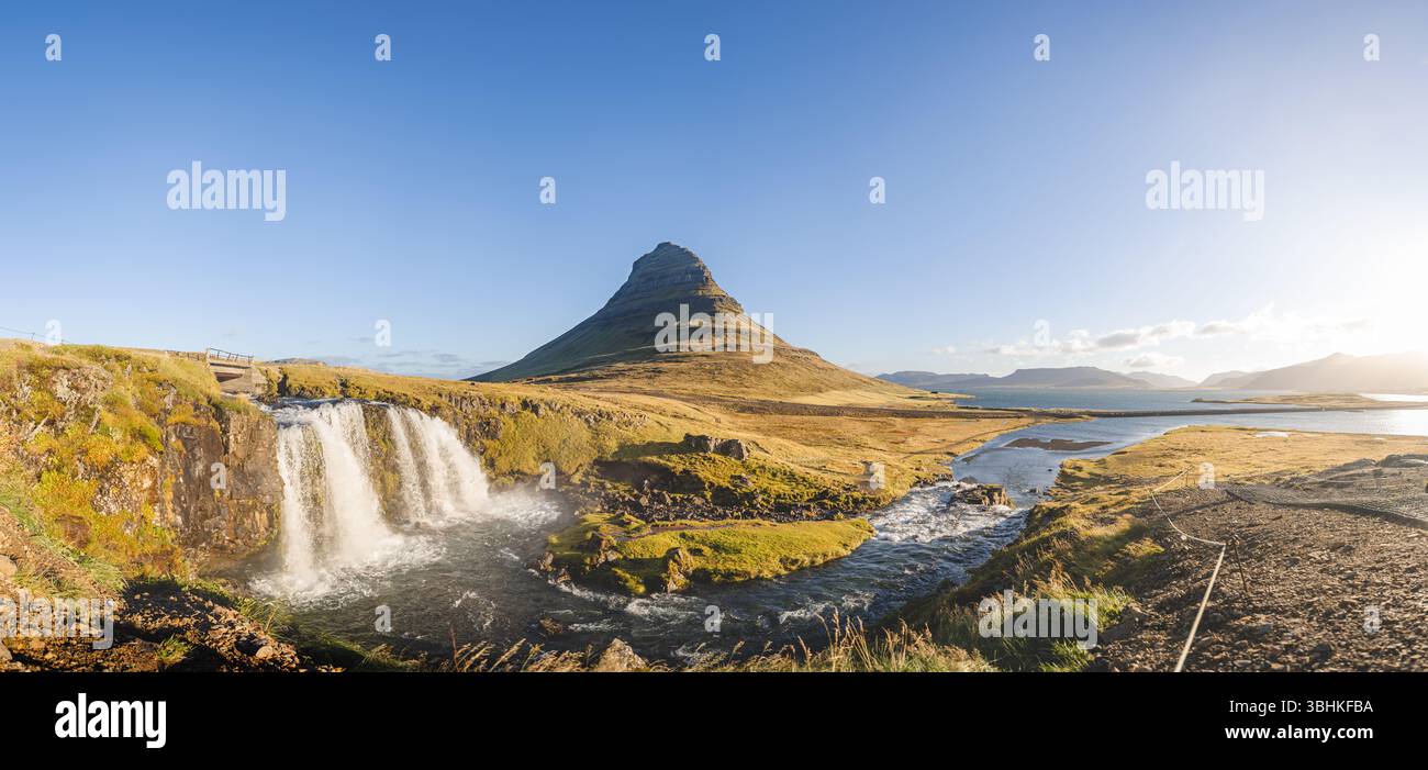 Kirkjufell mountain at sunrise with golden grasslands and soft clouds ...