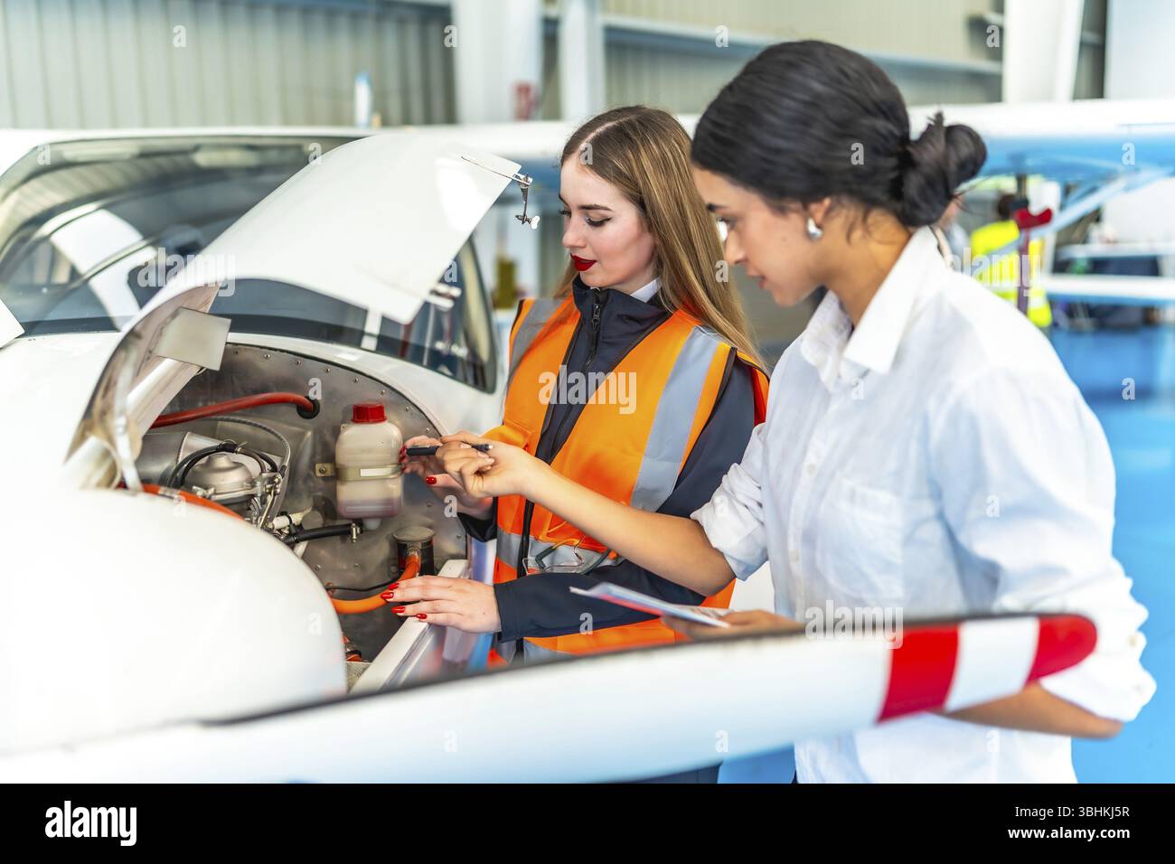 Two female engineers in a hangar inspecting an aircraft engine, focusing on maintenance and ...