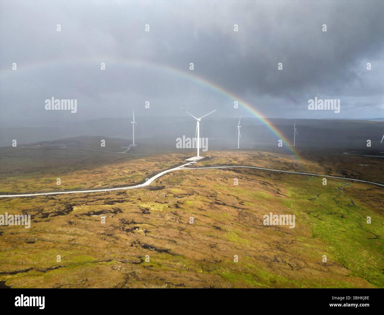 Drone shot of wind turbines beneath a vibrant rainbow with rain ...