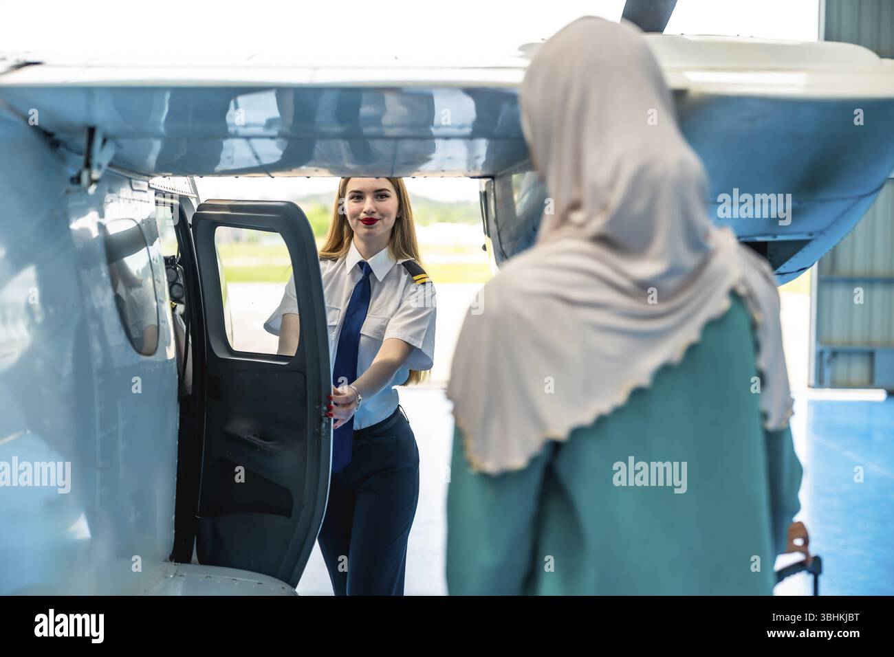 Female pilot welcoming a muslim passenger aboard a small airplane ...