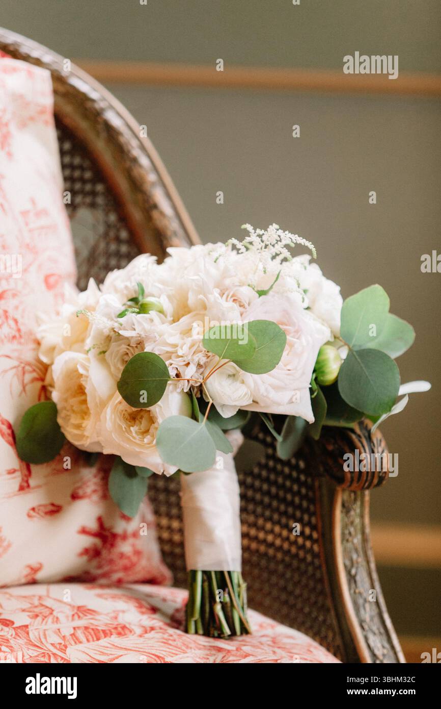 A beautiful bridal bouquet featuring white roses and greenery is placed ...