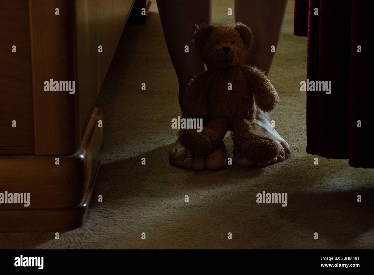Teddy bear on the feet of a girl standing barefoot on a carpet near a ...