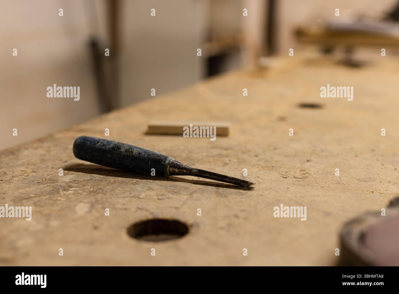 Metal-bladed chisel resting near drilled hole on sawdust strewn ...