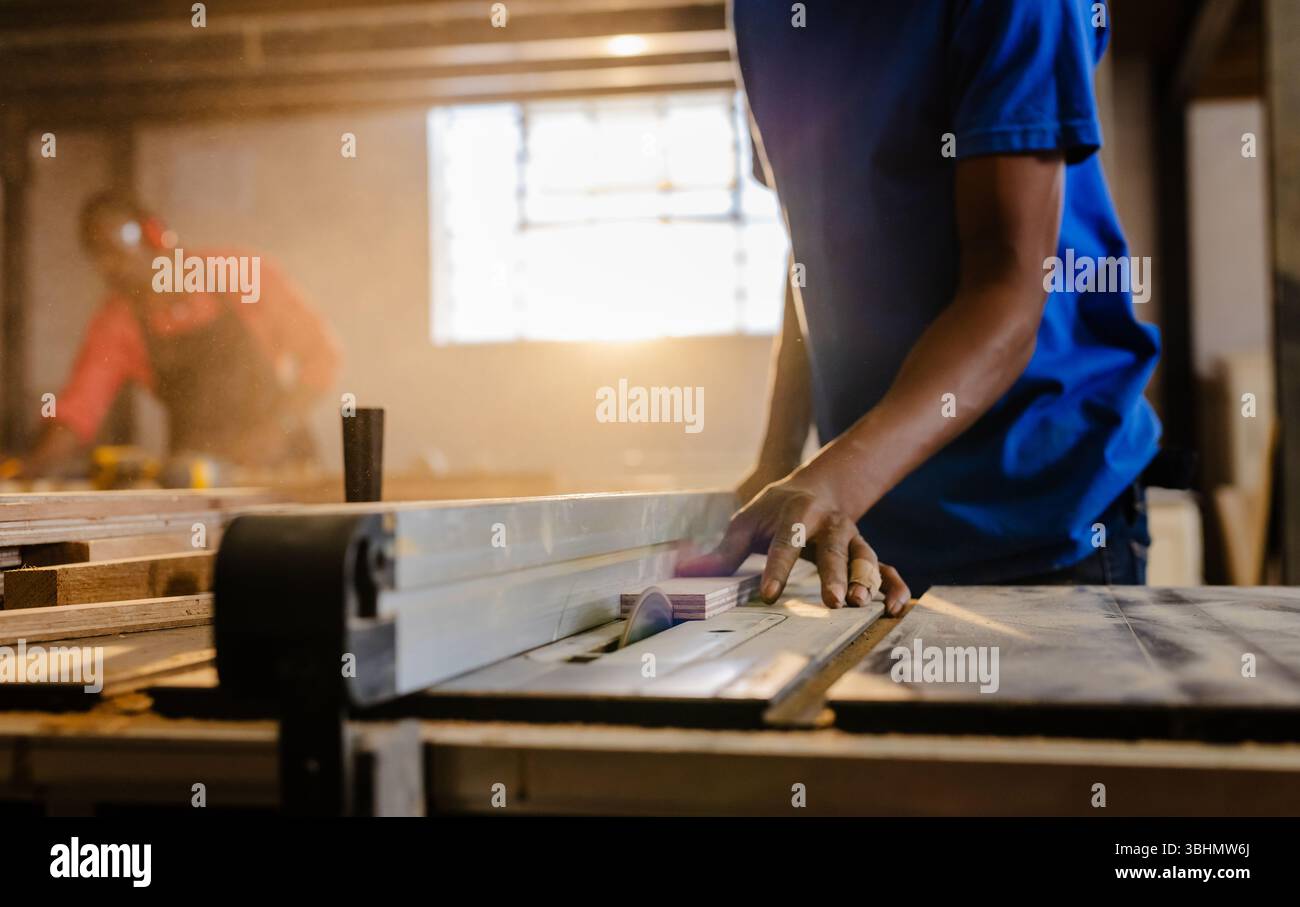 African American male coworkers operating table saw and sanding plank ...