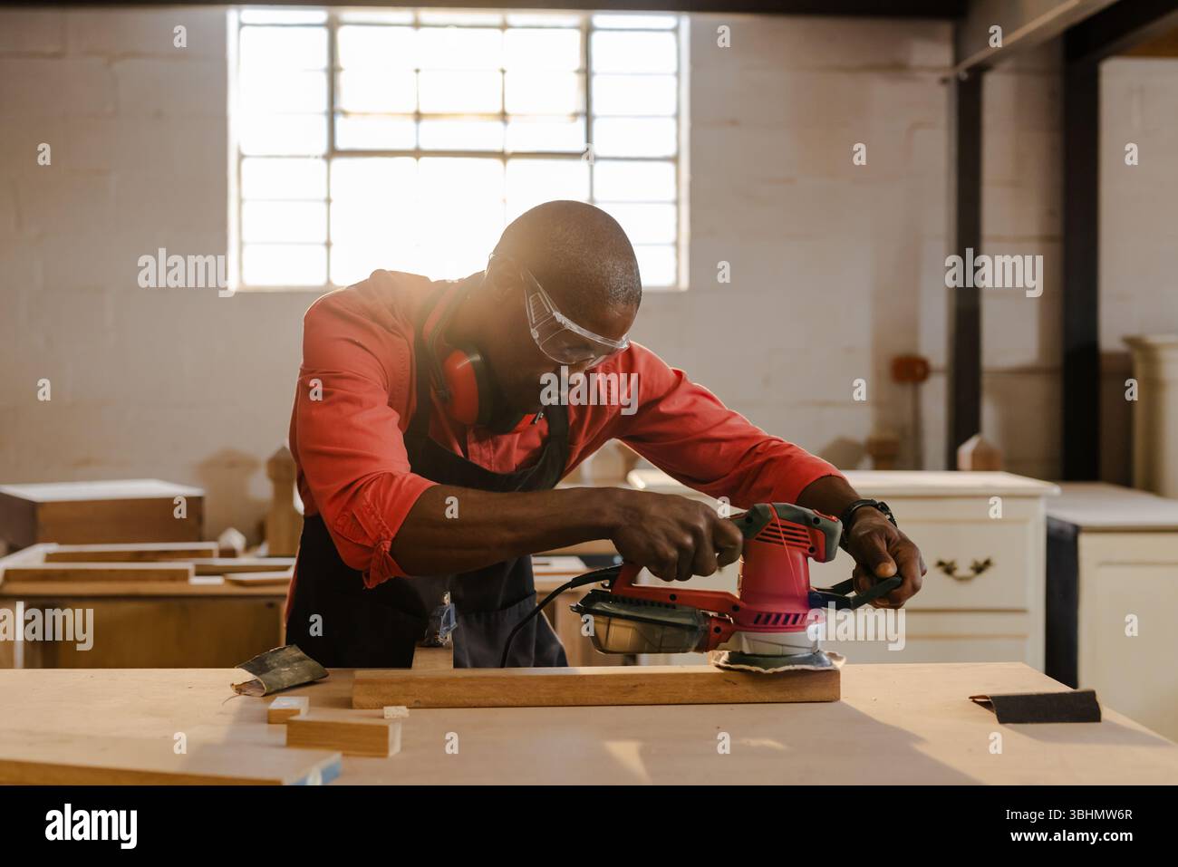 Electric orbital sander sanding wooden plank on workbench in bright ...