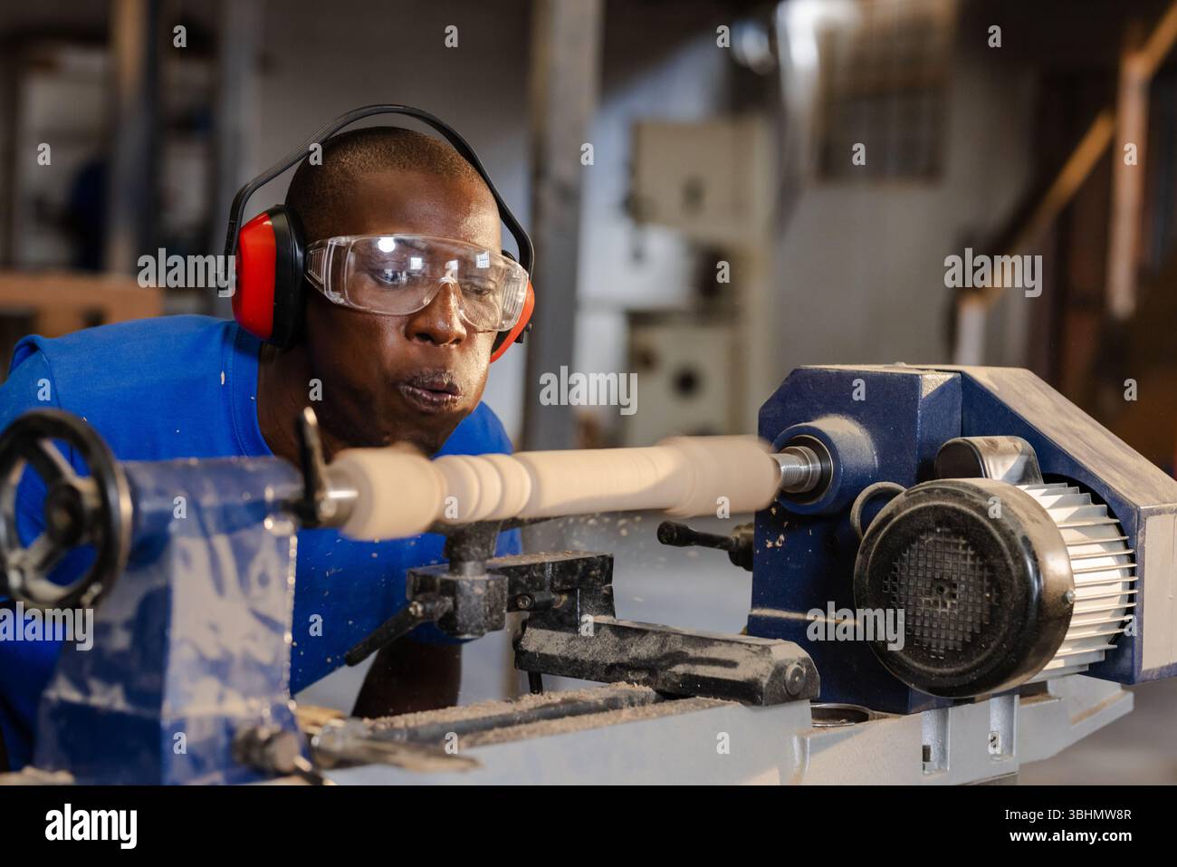 African American man in coveralls turning lathe spindle in workshop ...