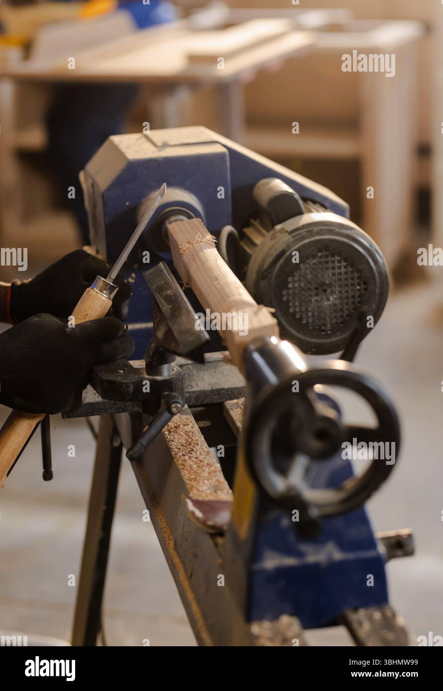 Wood lathe rotating wooden blank in workshop, with gloved hands carving ...