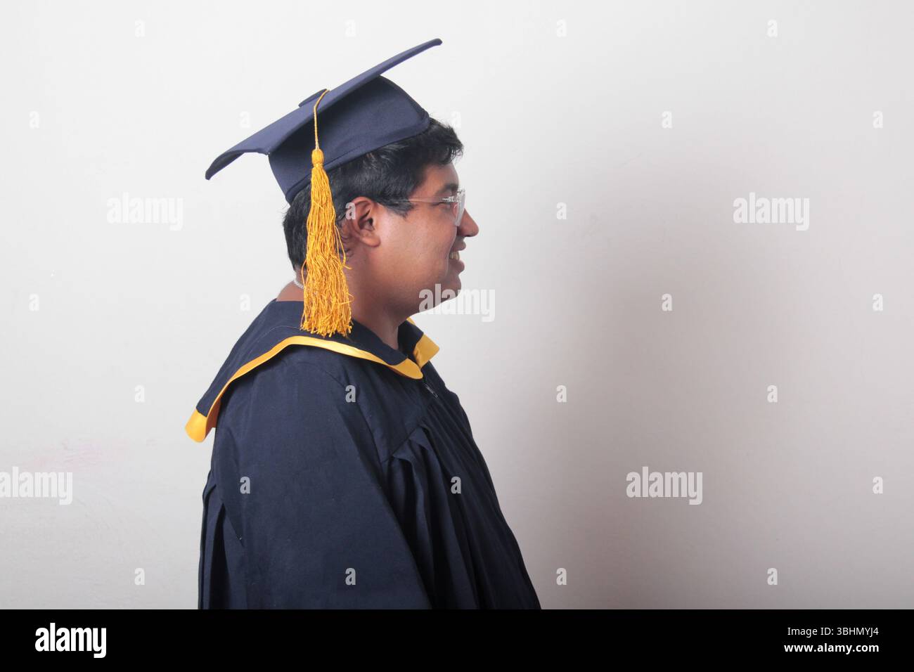 30-year-old dark-skinned Latino man with glasses wears a cap and gown ...