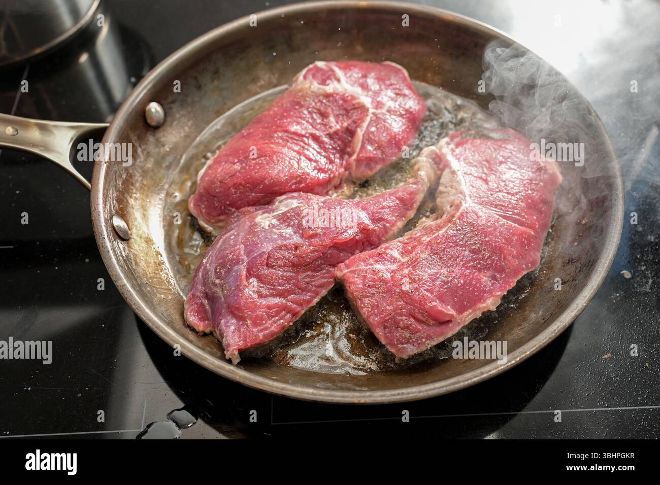 Fresh raw beef steaks are seared in hot oil with plenty of steam in a ...