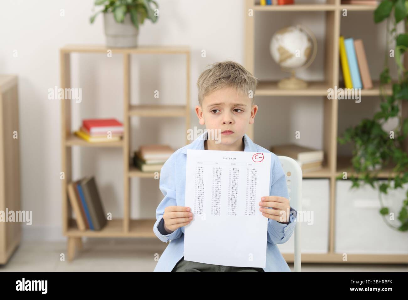 School grade. Sad boy holding answer sheet with letter F indoors Stock ...