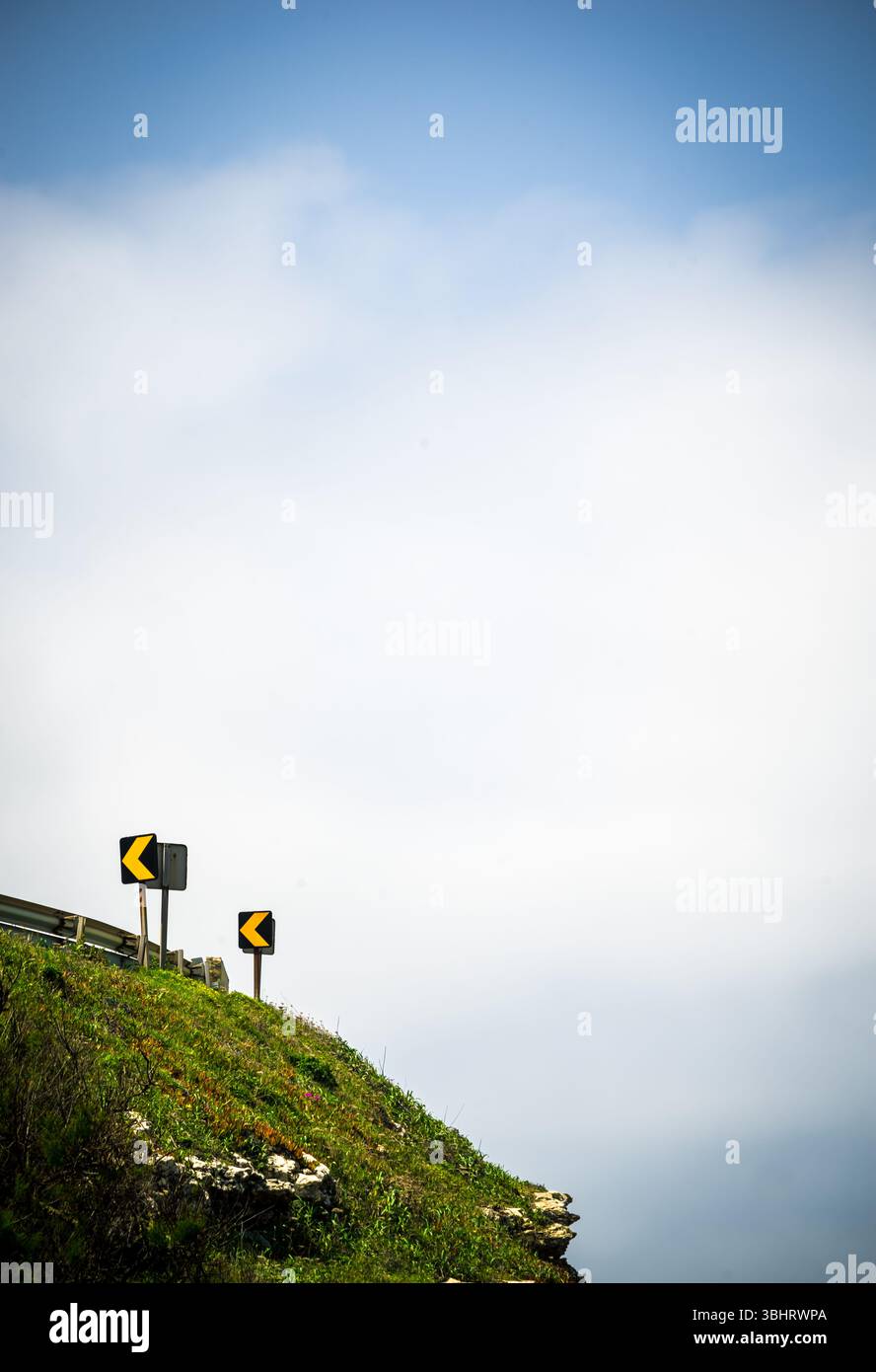 Yellow warning road signs indicating sharp curve ahead on grassy hillside symbolizing importance ...