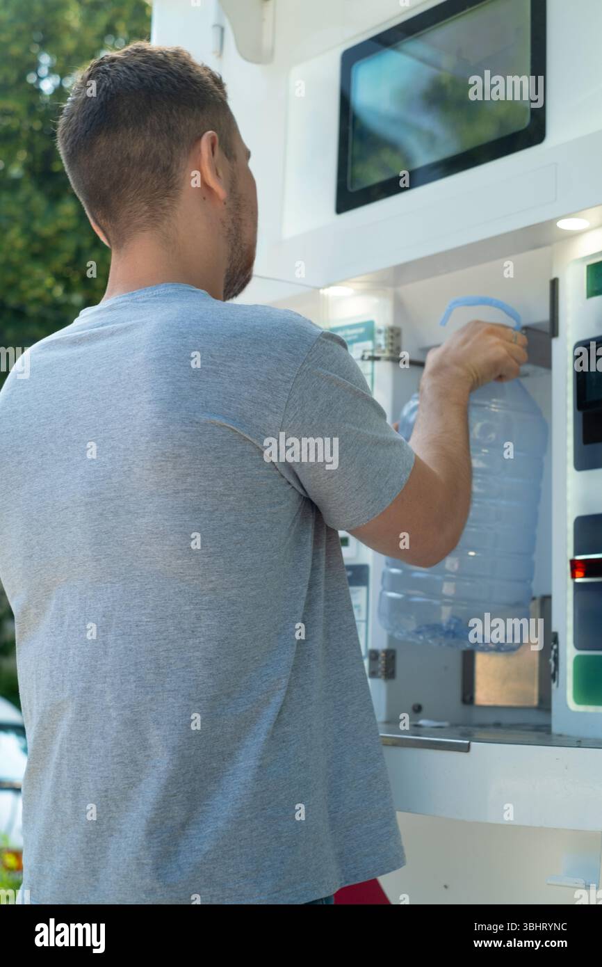 Man filling plastic container with drinking water from water vending ...