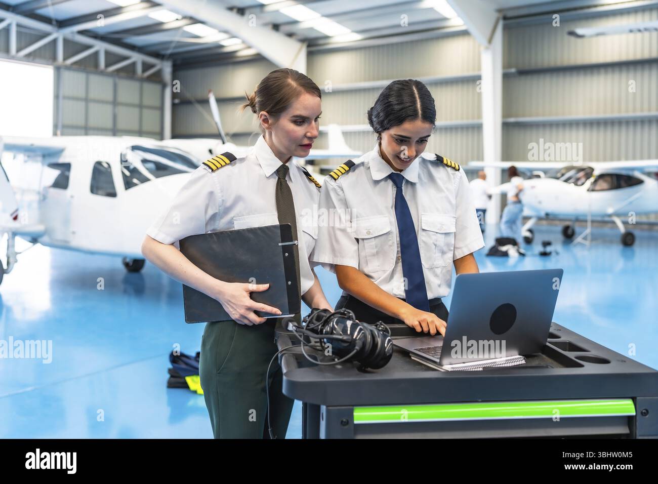 Two smiling female pilots in uniform working on a laptop inside a ...
