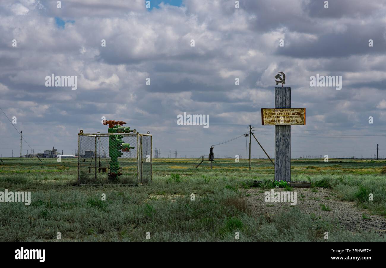 The photo shows a steppe landscape with an oil wellhead fenced with ...
