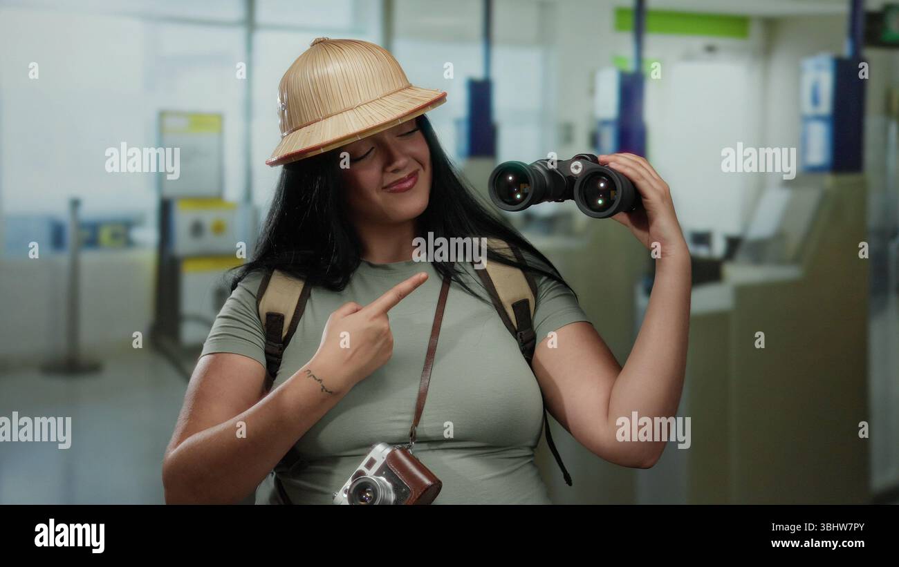 Woman in airport terminal holding binoculars wearing safari hat and ...