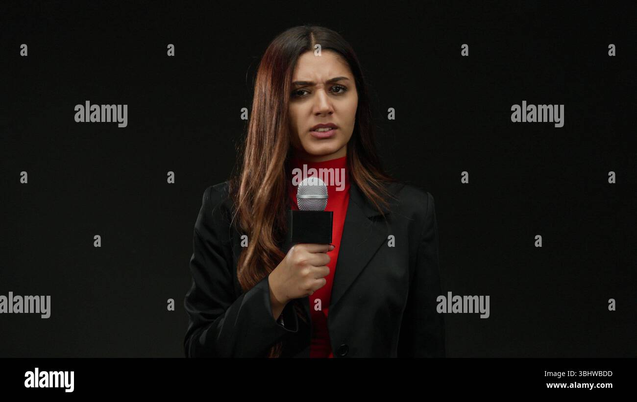 Woman reporter holding microphone against isolated black background ...