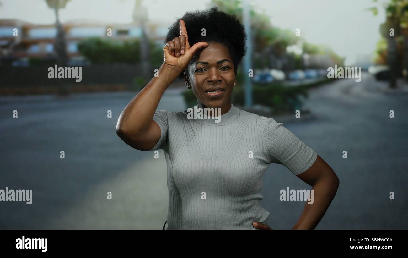 Woman making loser gesture outdoors in city street, african descent ...
