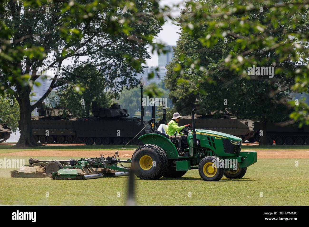 A landscaper mows the grass of a baseball field as M1 Abrams tanks and ...
