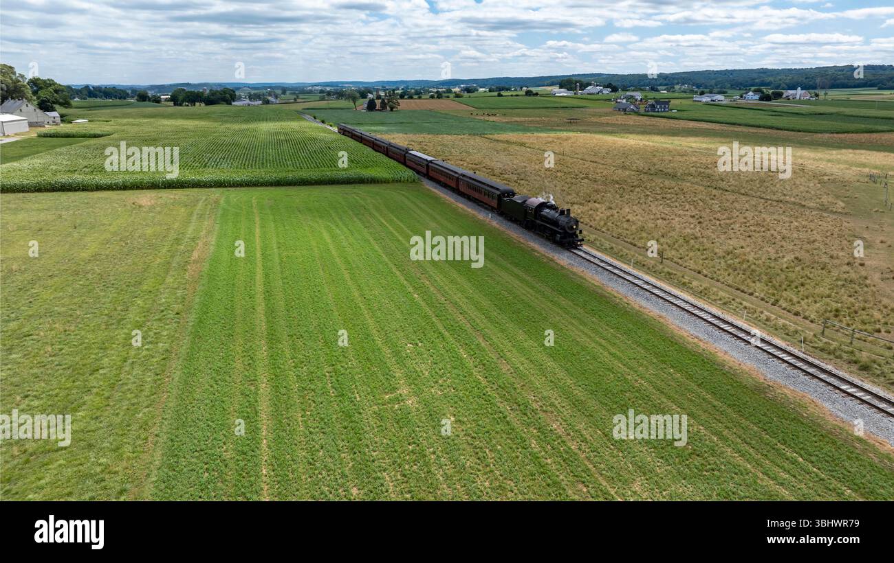 A steam train moves along railway tracks surrounded by expansive green ...