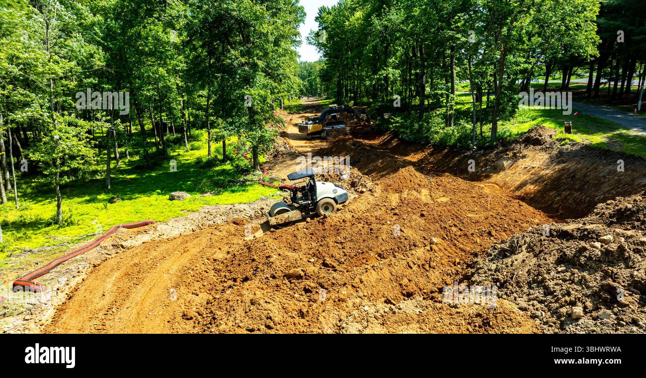 Heavy machinery operates in a forested area, moving dirt and reshaping ...