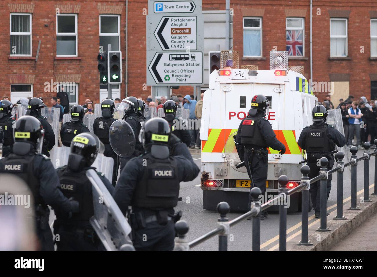 Police in riot gear form a protective line as a crowd gathers in ...