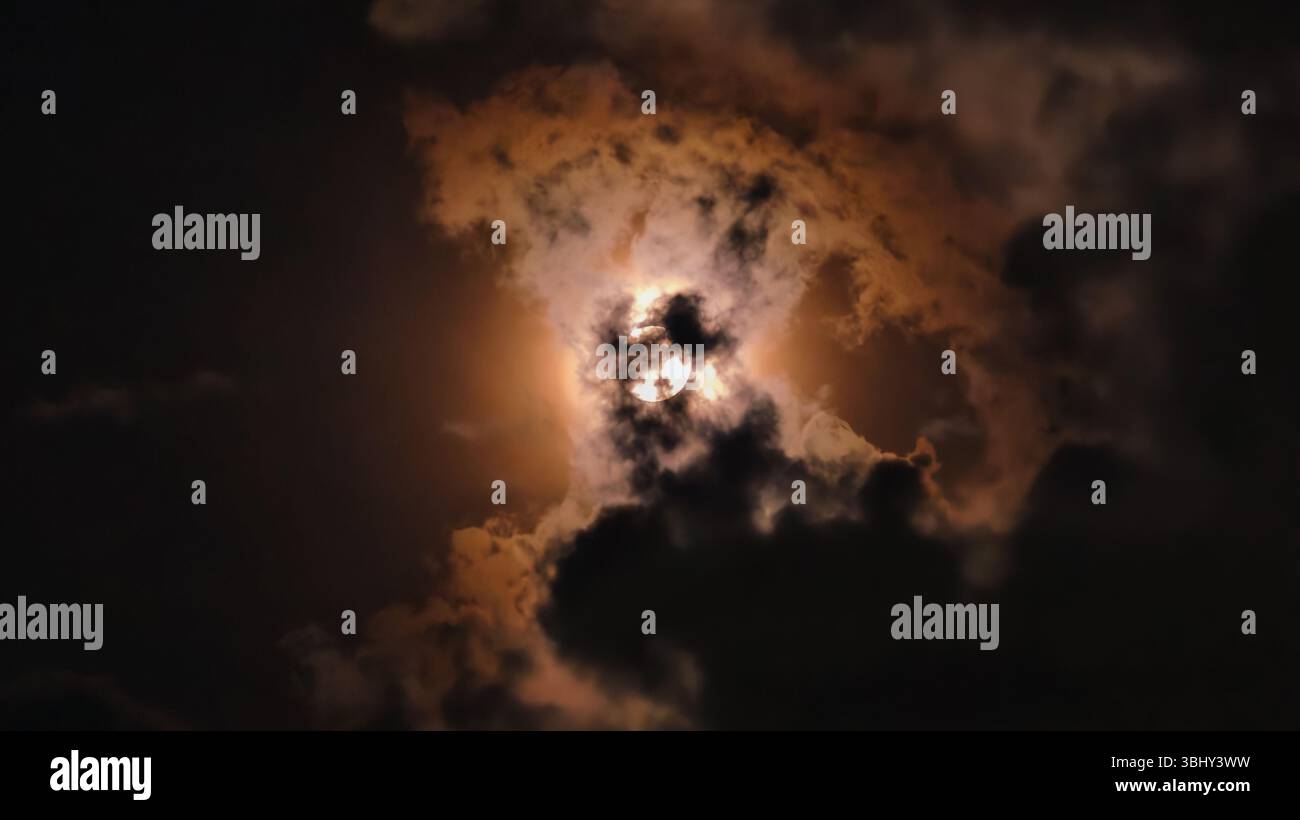 Full moon partially obscured by dark dramatic clouds in the night sky ...