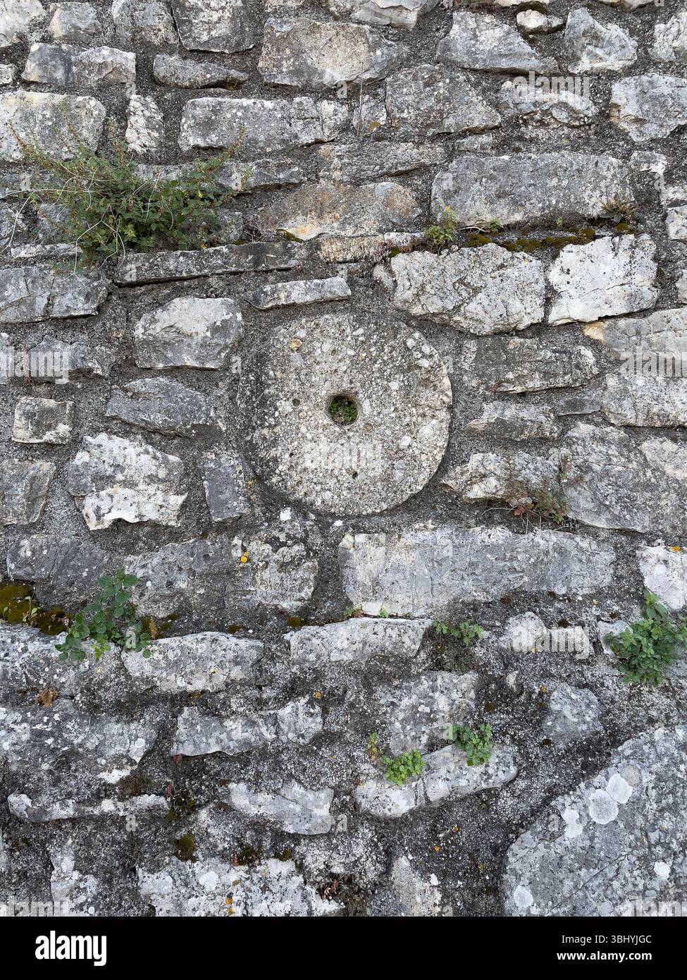 Old masonry wall made of rugged stones with a circular stone element ...