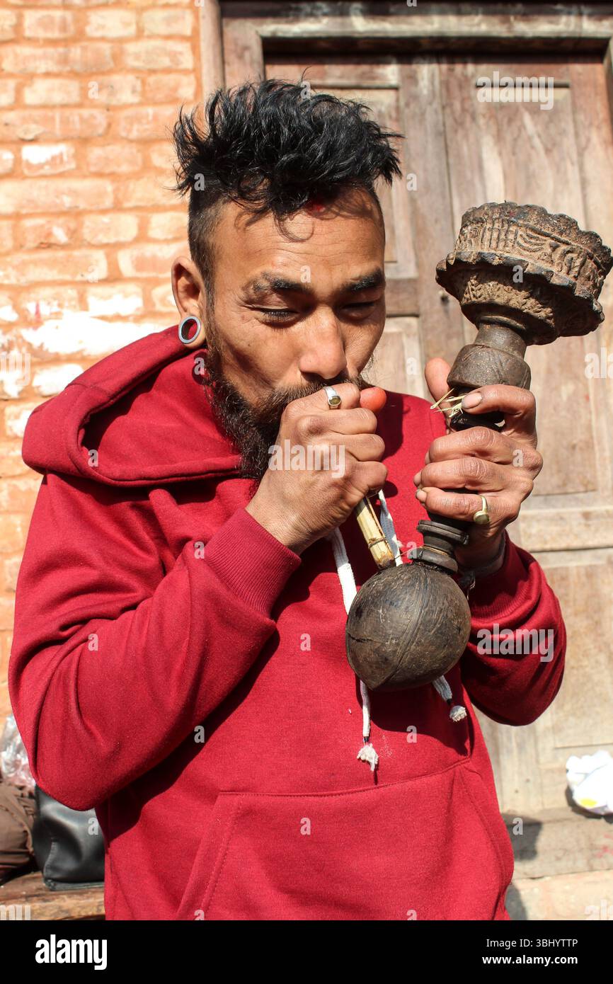 A Newar man preparing his traditional clay hookah at the Hanuman Ghat ...
