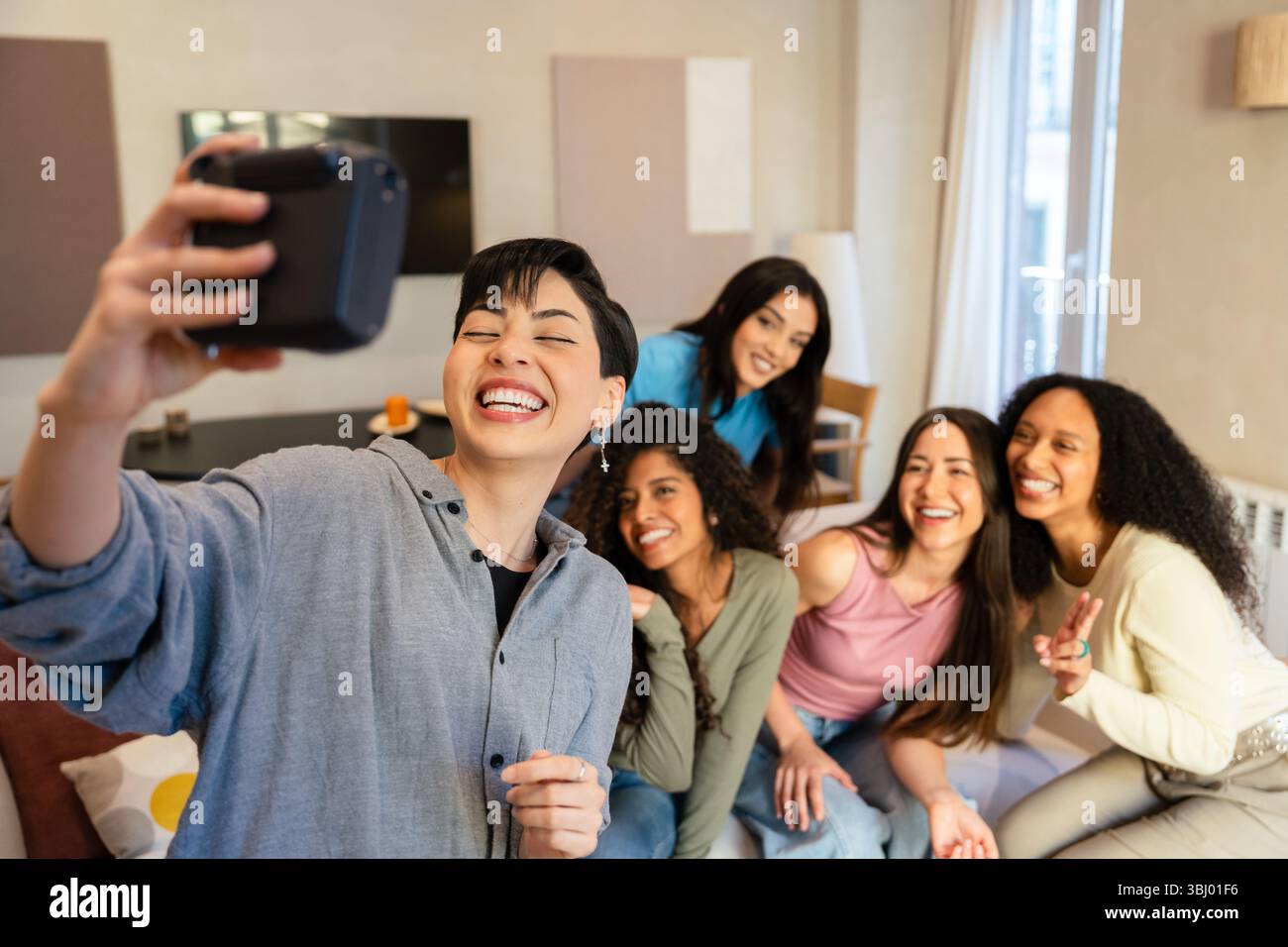 A group of five diverse friends gather indoors, smiling and capturing a ...