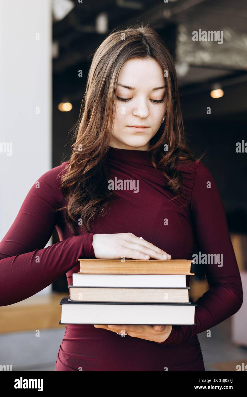 A female student in a maroon dress stands thoughtfully in an academic ...