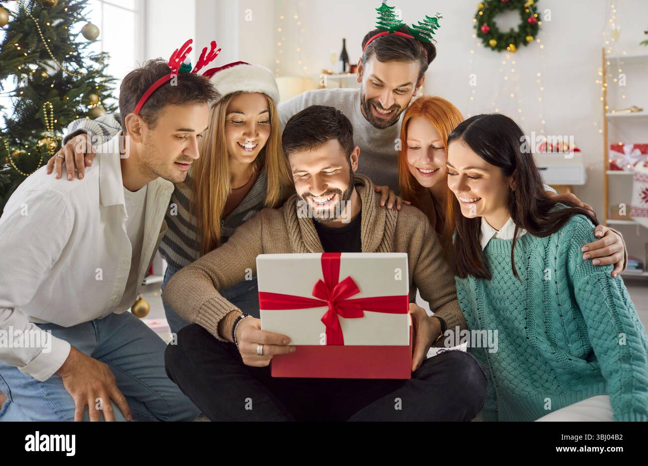 Happy friends gathering around mate opening gift box, celebrating ...