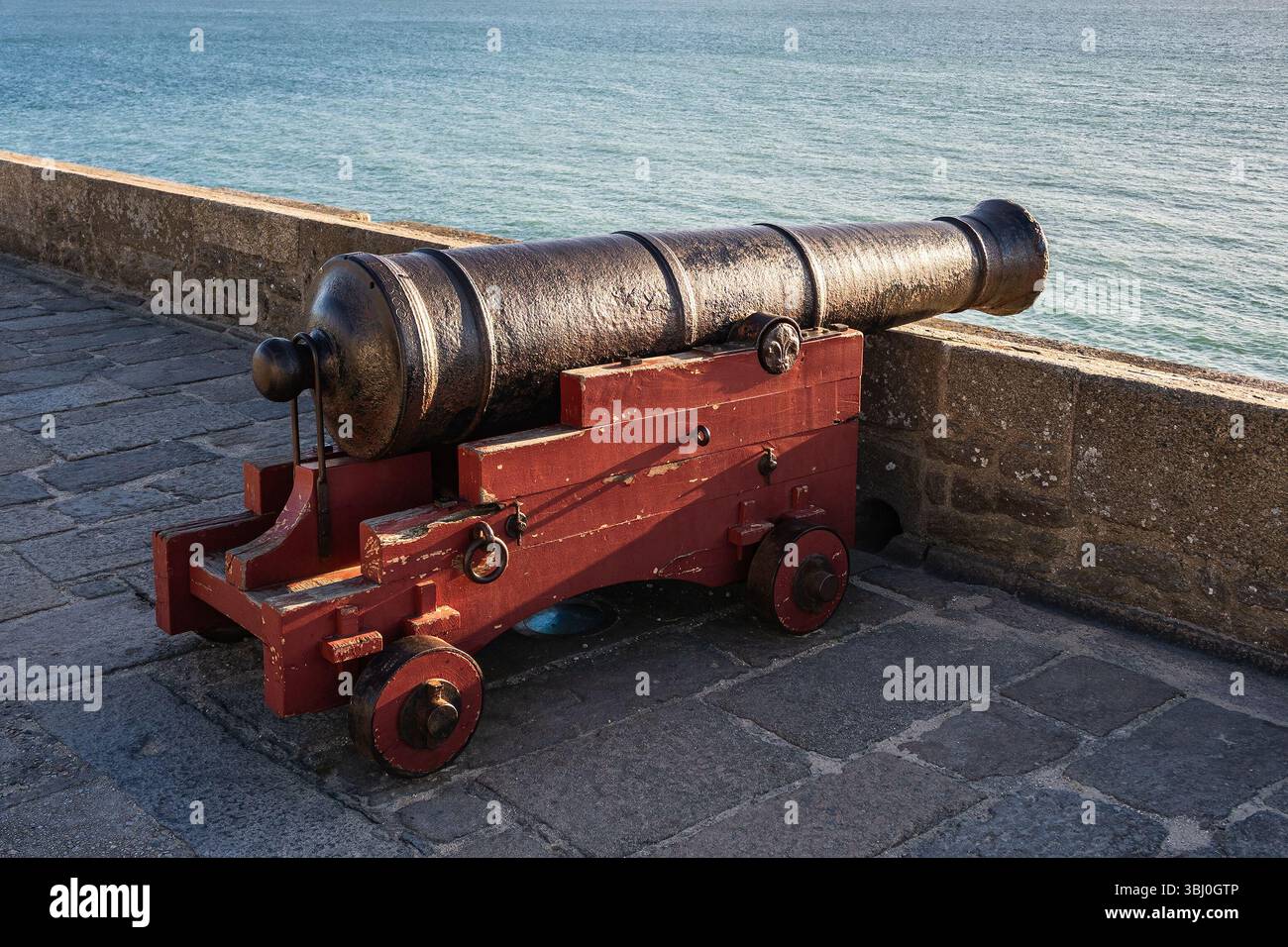 Old iron cannon on red wooden carriage atop the stone ramparts of Saint ...