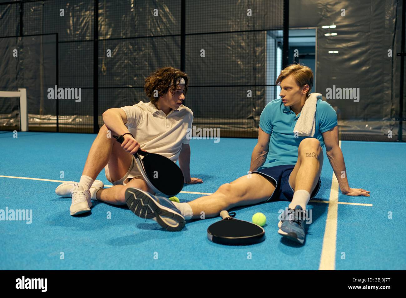 Two young athletes relax on the padel court, chatting after an ...
