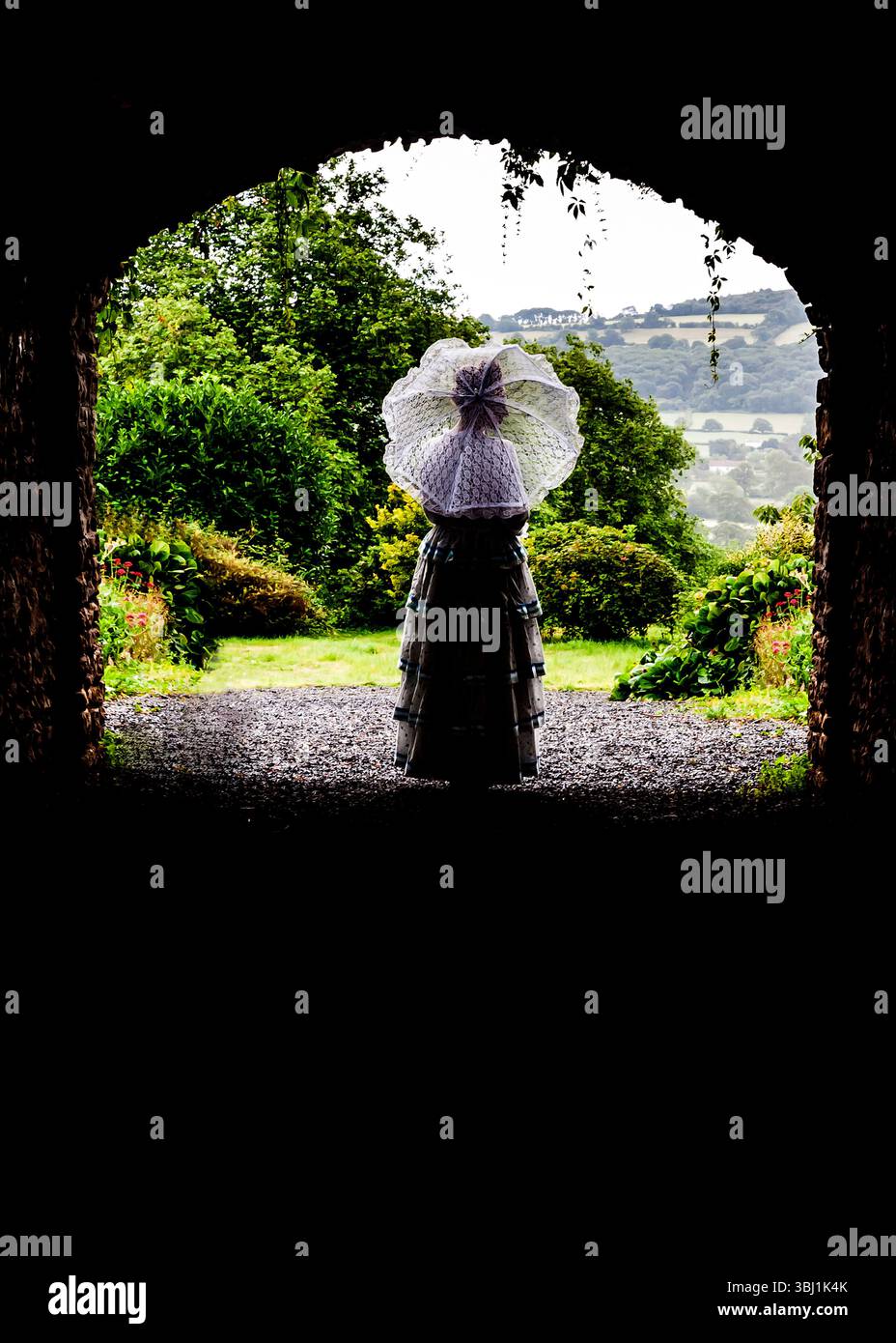 A person in a long dress and holding a lace parasol stands in the ...