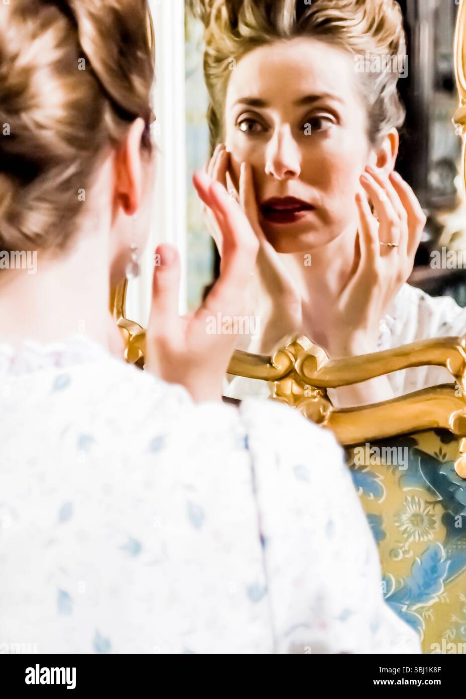 A woman looks at her reflection in a mirror, touching her face with ...