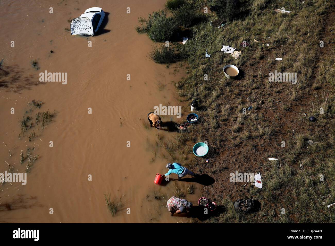 Women wash their clothes along the river next a car that was swept ...