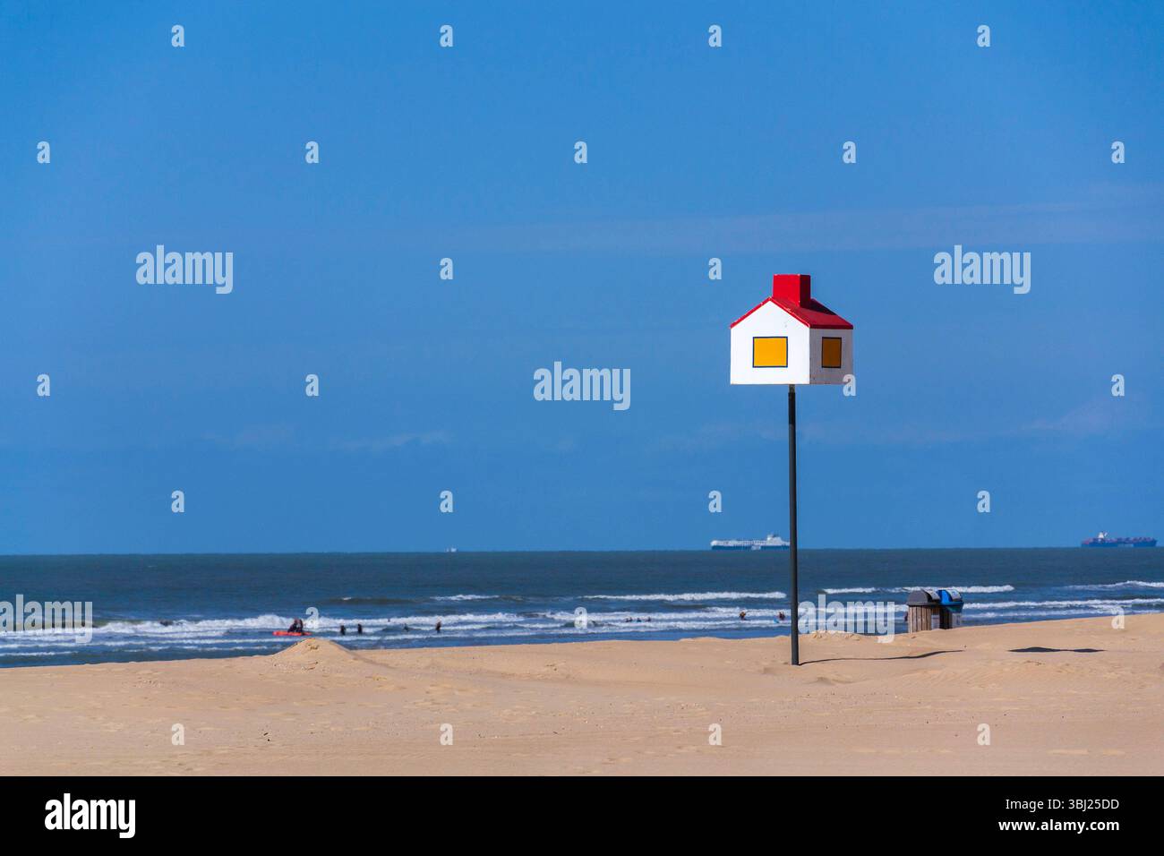 Wooden model of a house with a red roof on a pole on a sandy beach ...