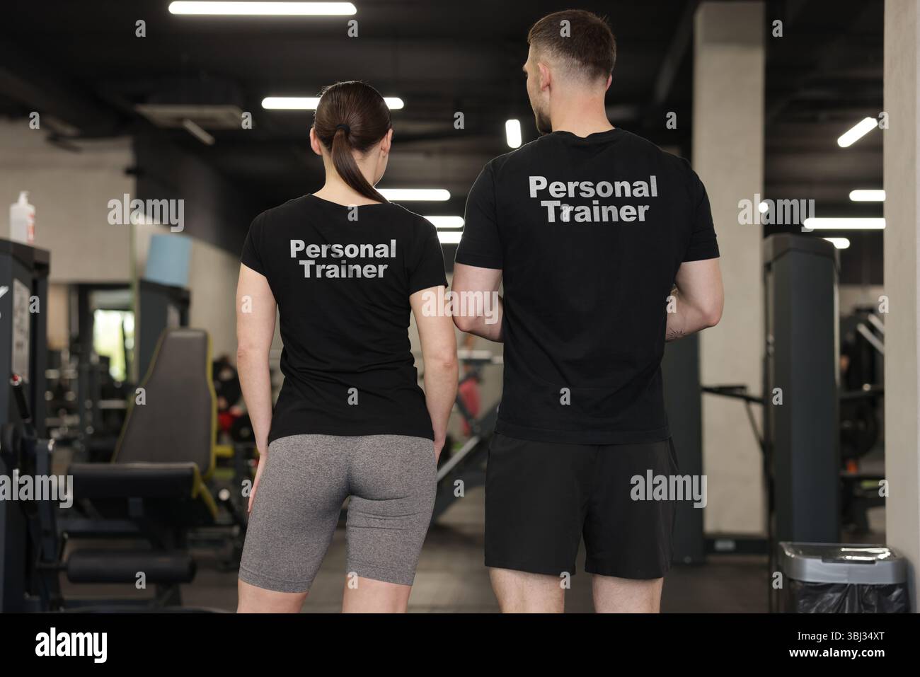 Personal trainers wearing t-shirts with inscriptions in gym. Back view ...