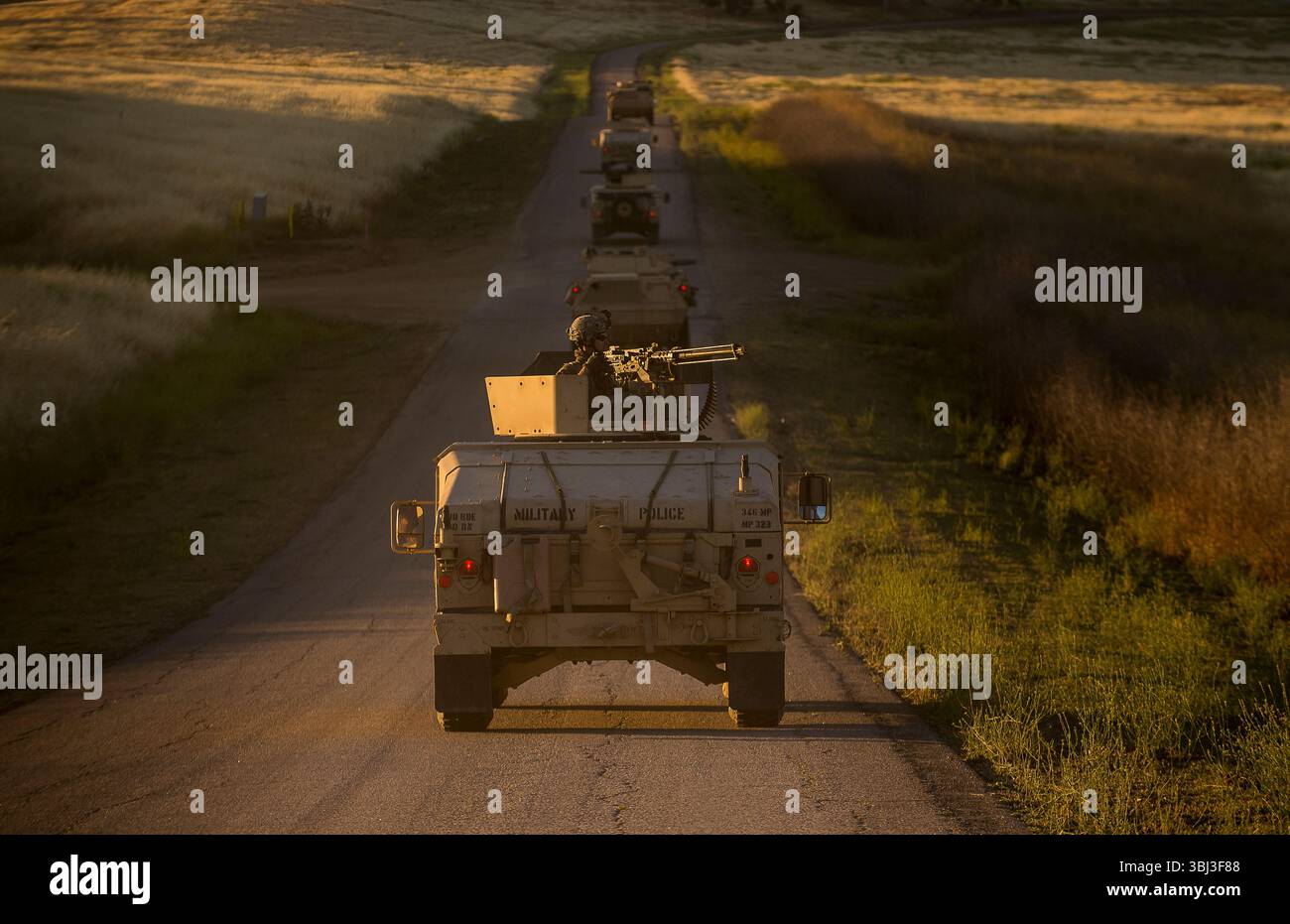 A U.S. Army HMMWV convoy drives in a straight line at sunrise through ...