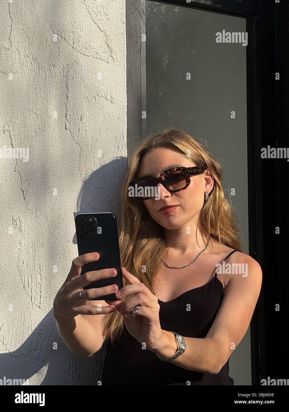 Woman taking a selfie in bright sunlight by an outdoor wall in urban ...