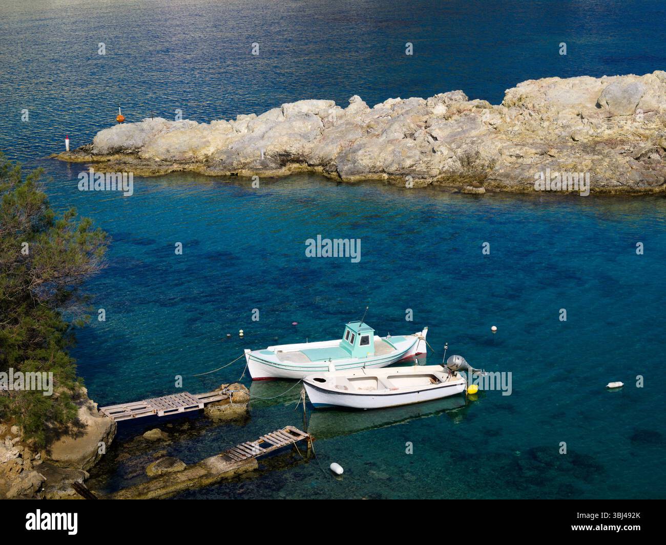 Two small boats rest on calm turquoise water near a rock formation. A ...