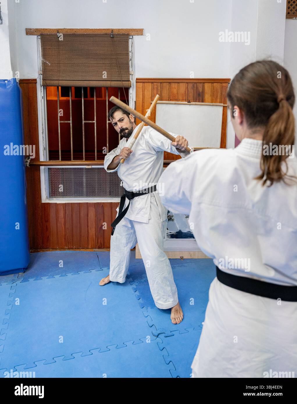 Two karate athletes practicing with wooden training weapons inside dojo ...