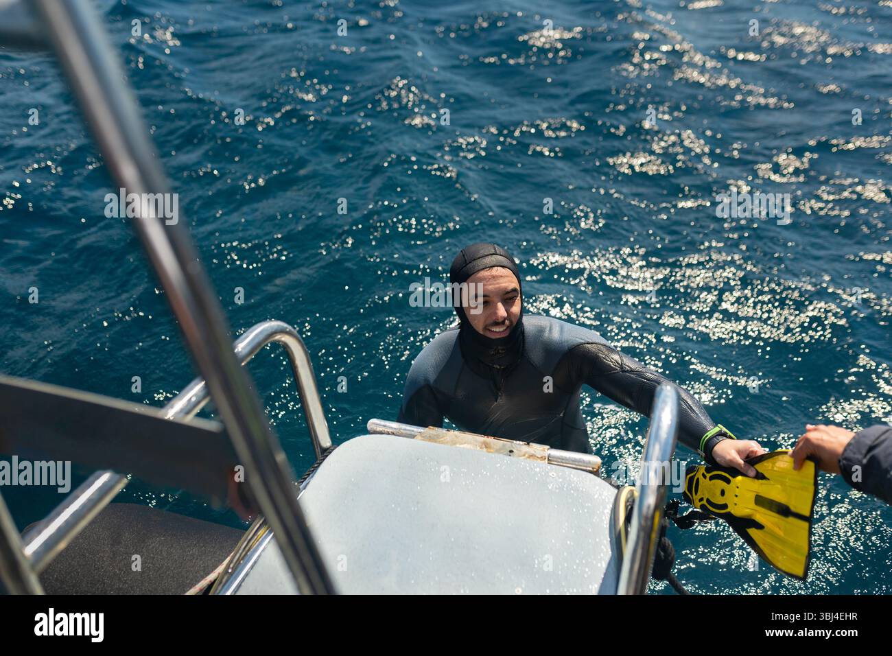 Diver wearing a wetsuit getting ready to dive from boat assisted by ...