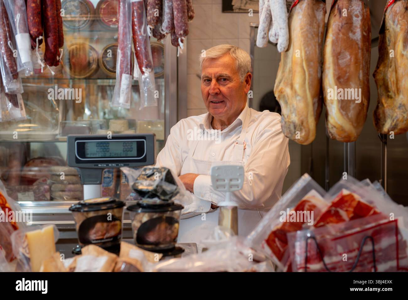 Senior butcher standing with arms crossed behind his counter in a ...