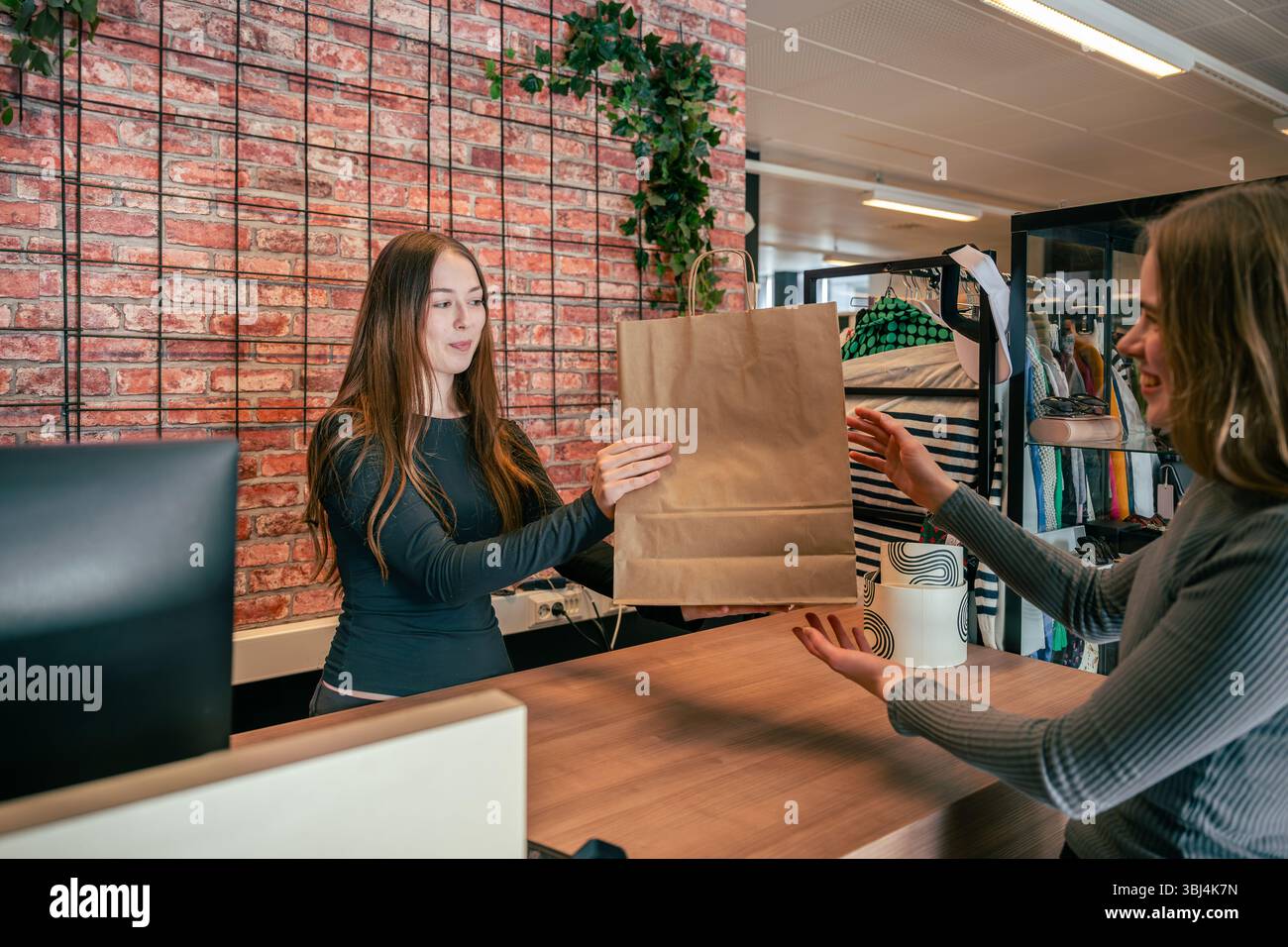 Female shop assistant giving paper bag to customer in clothing store ...