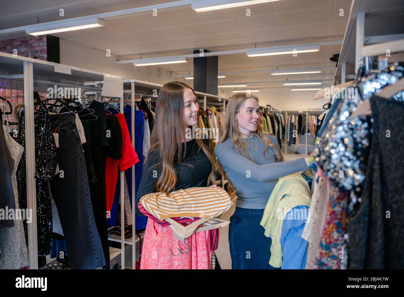 Two young women browsing clothes at second hand clothing store Stock ...